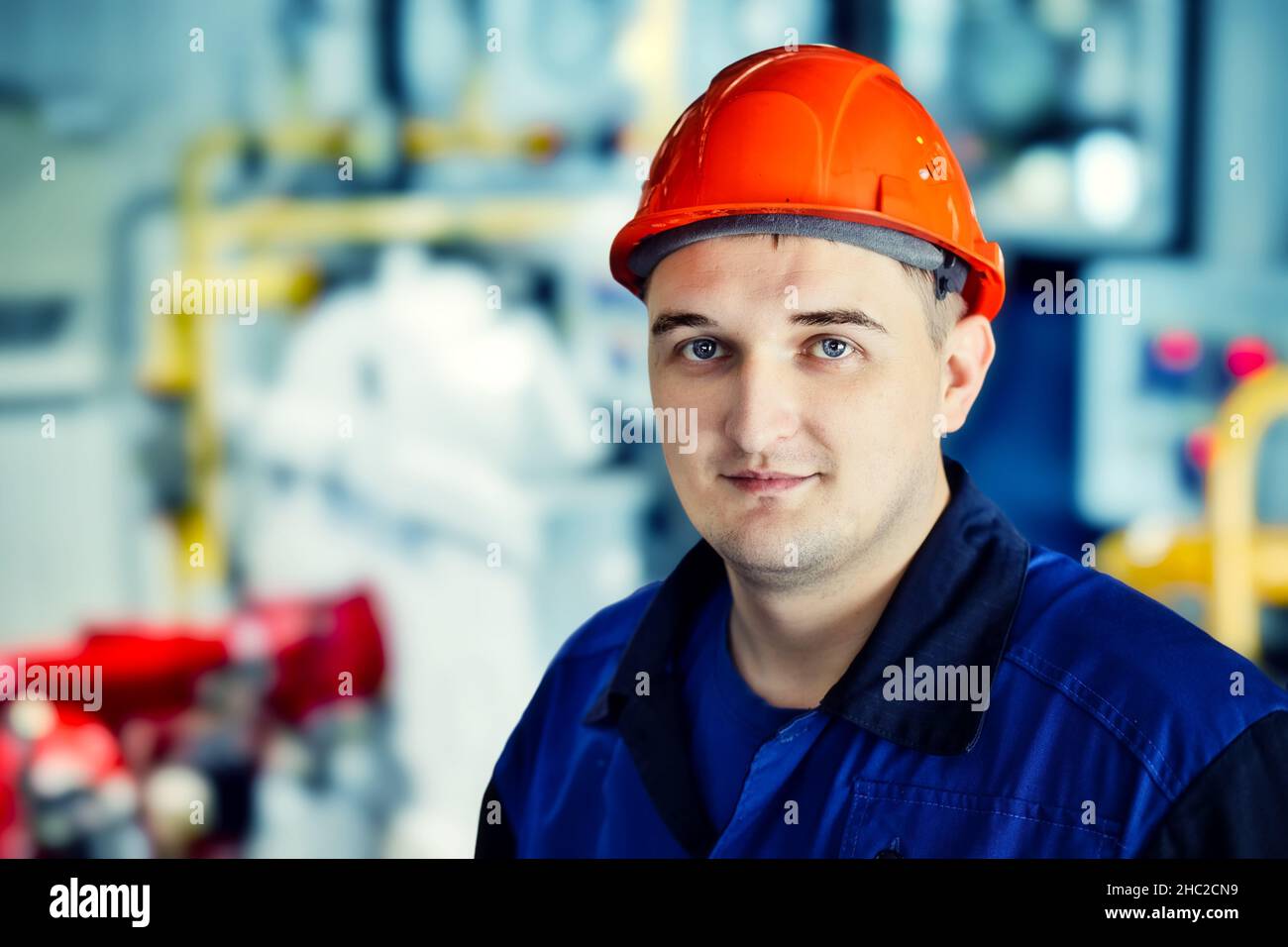 Portrait of young engineer in helmet in working environment at factory ...