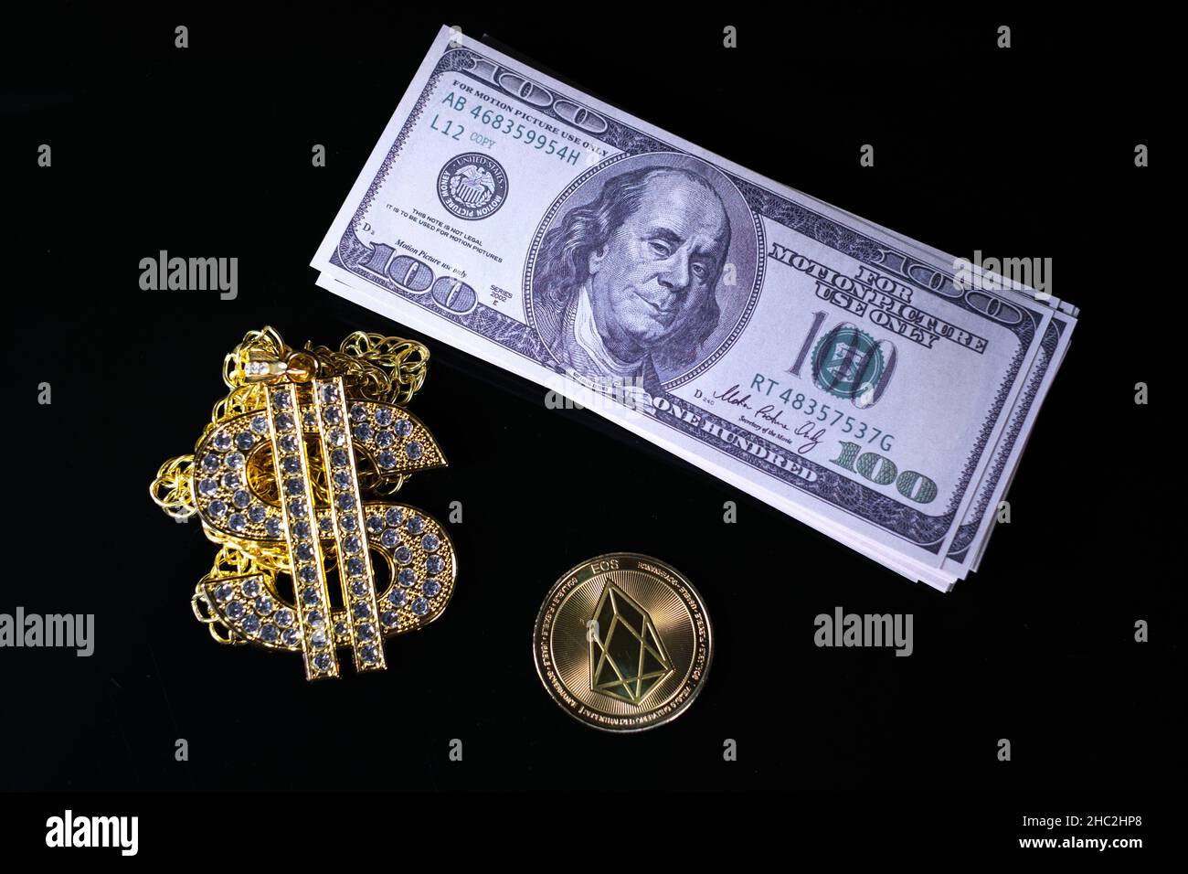 one EOS coin lying next to a stack of $100 bills and a diamond-studded ...