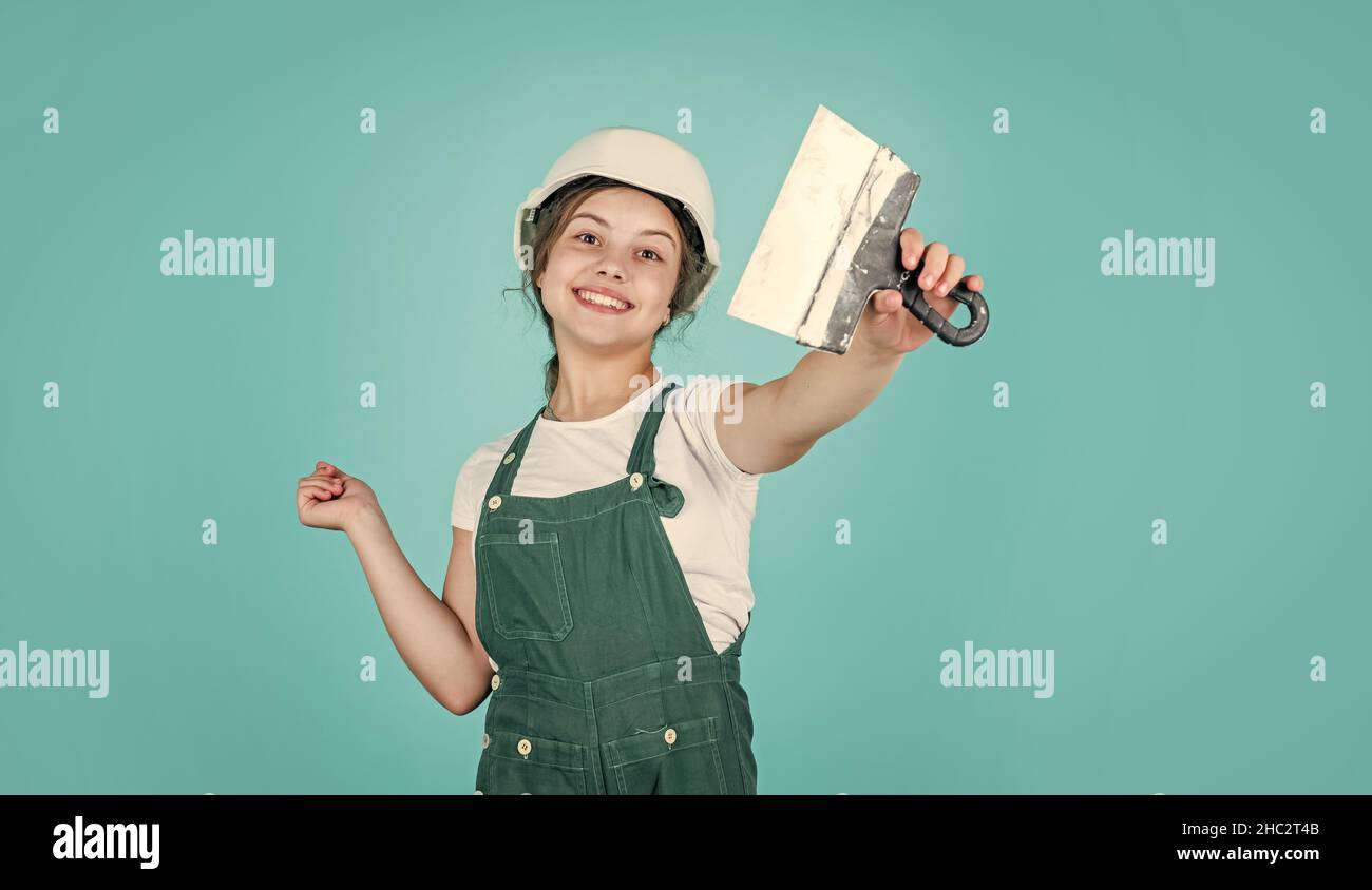 cheerful child laborer using building uniform and plastering spatula ...
