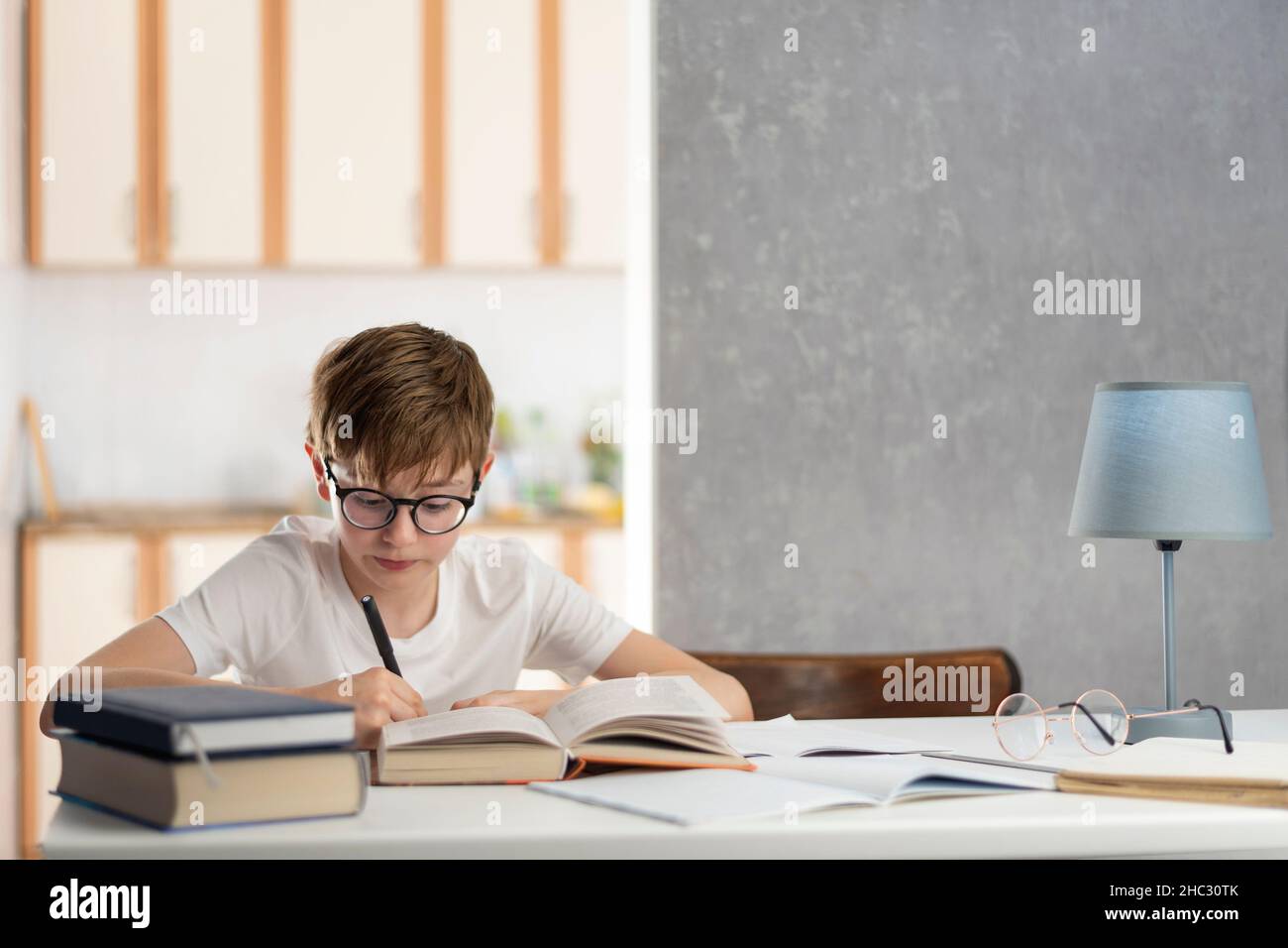 Boy with glasses does his homework. Teenage boy writes in a notebook ...