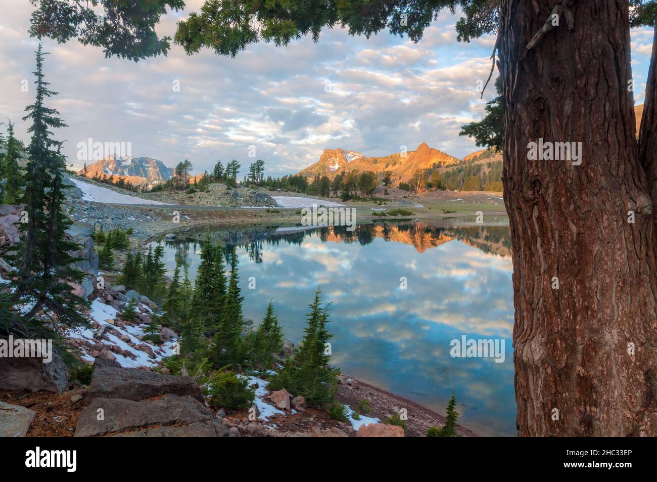 A serene mountain lake reflects the sky and surrounding peaks, creating ...