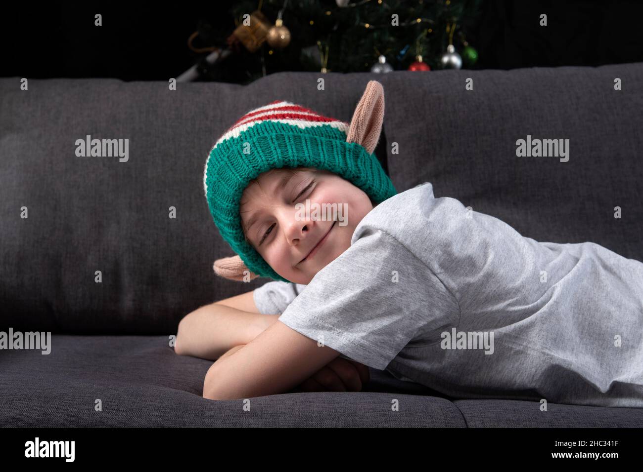Cute boy in christmas elf hat is resting on the sofa with closed eyes ...