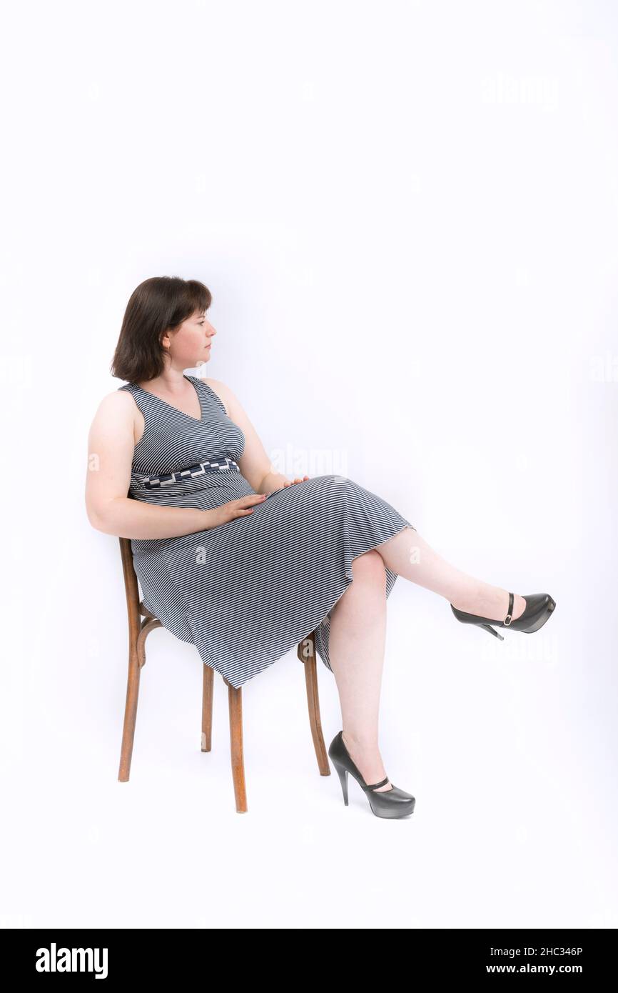 Plus size women in gray dress and heels sits on chair. Isolated on a ...