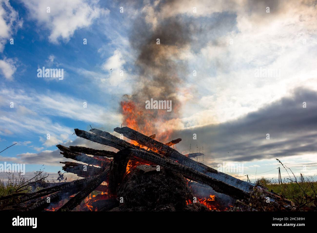 View of a large campfire with black smoke rising into the blue sky ...