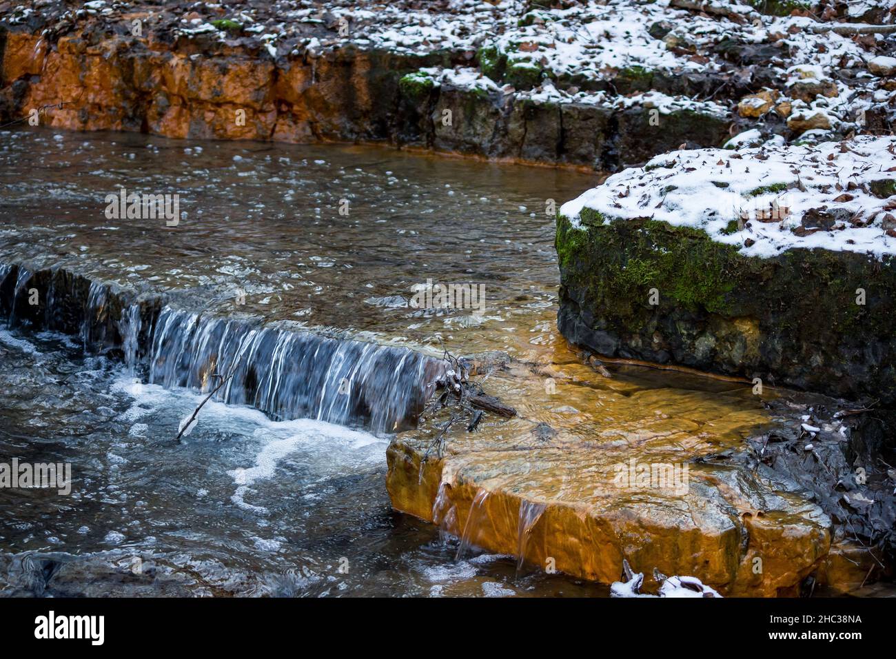 Small waterfalls on the river, limestone layers painted in orange with ...