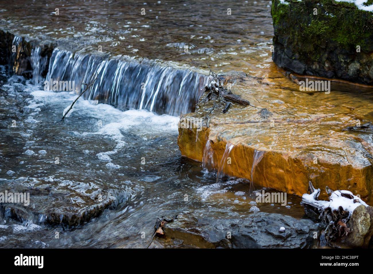 Small waterfalls on the river, limestone layers painted in orange with ...