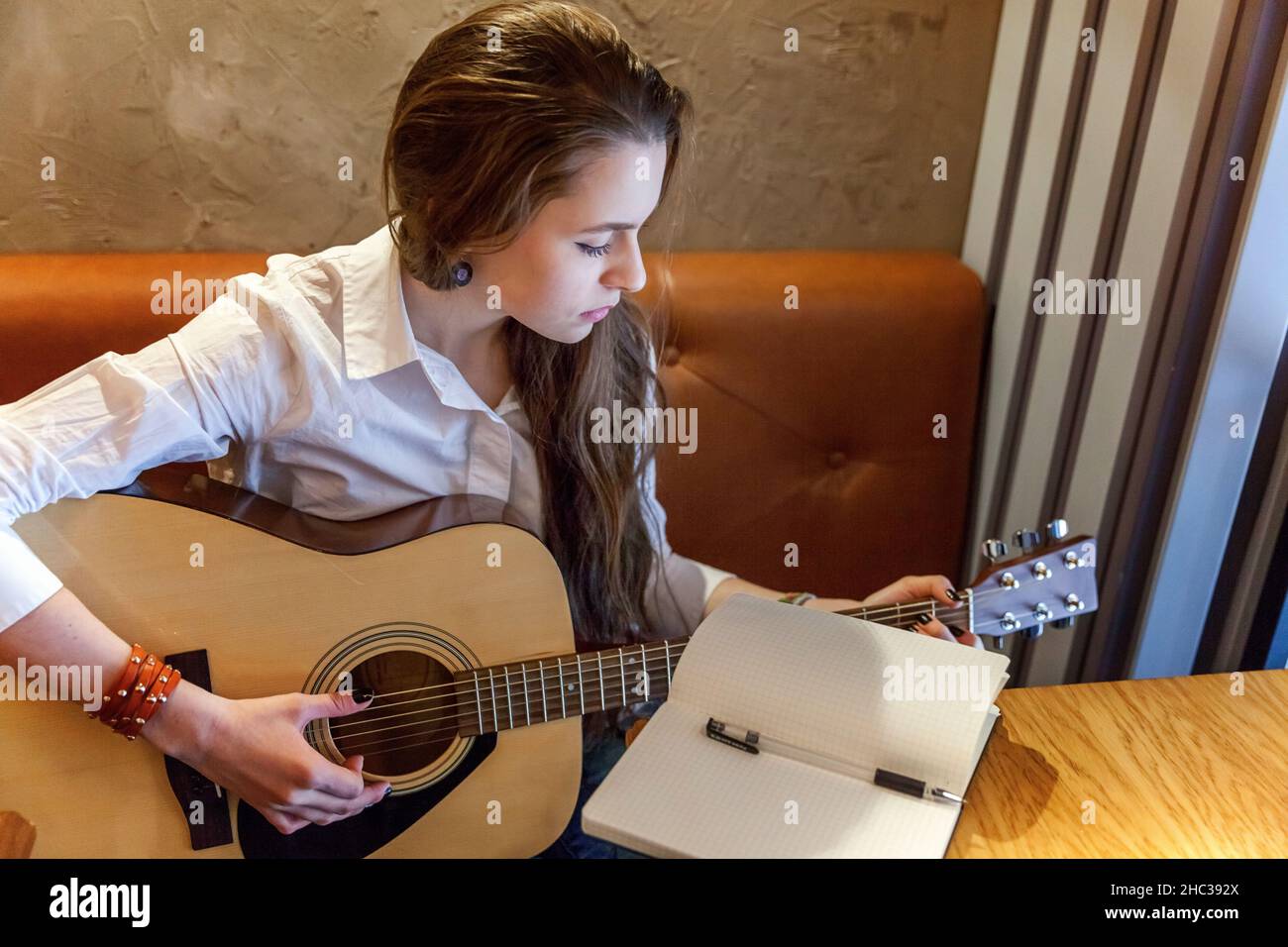 Young smiling hipster woman sitting playing guitar and write a song at ...