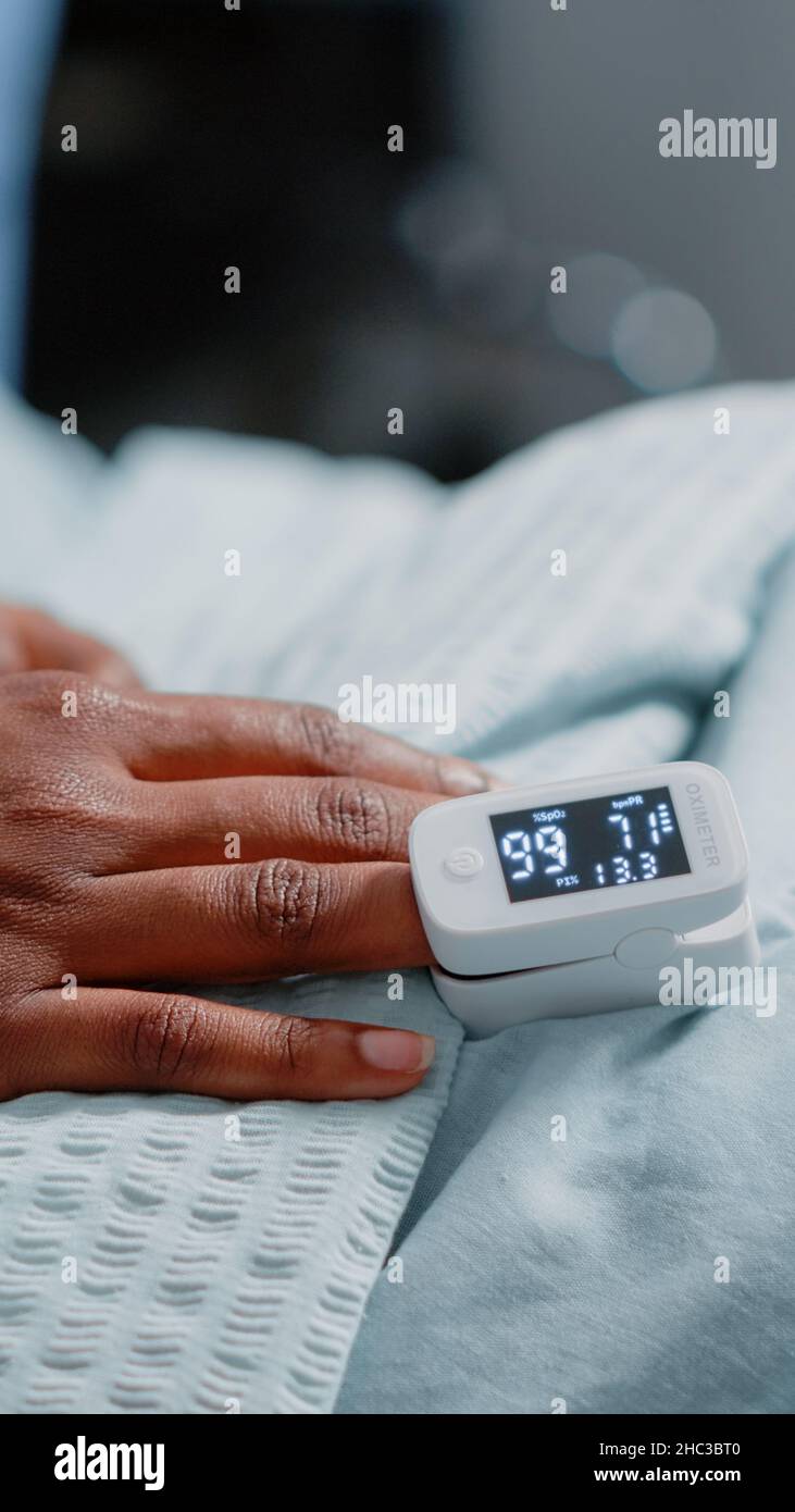 Close up of oximeter on finger of patient with illness in hospital ward ...