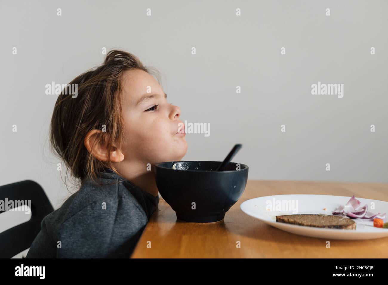 Unhappy child girl eats soup from black bowl with bread and onion ...
