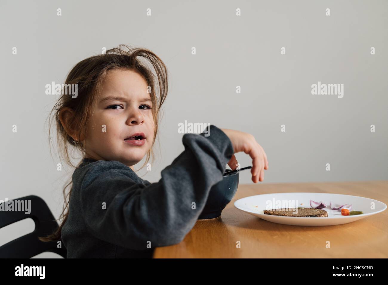 Unhappy child girl eats soup from black bowl with bread and onion ...