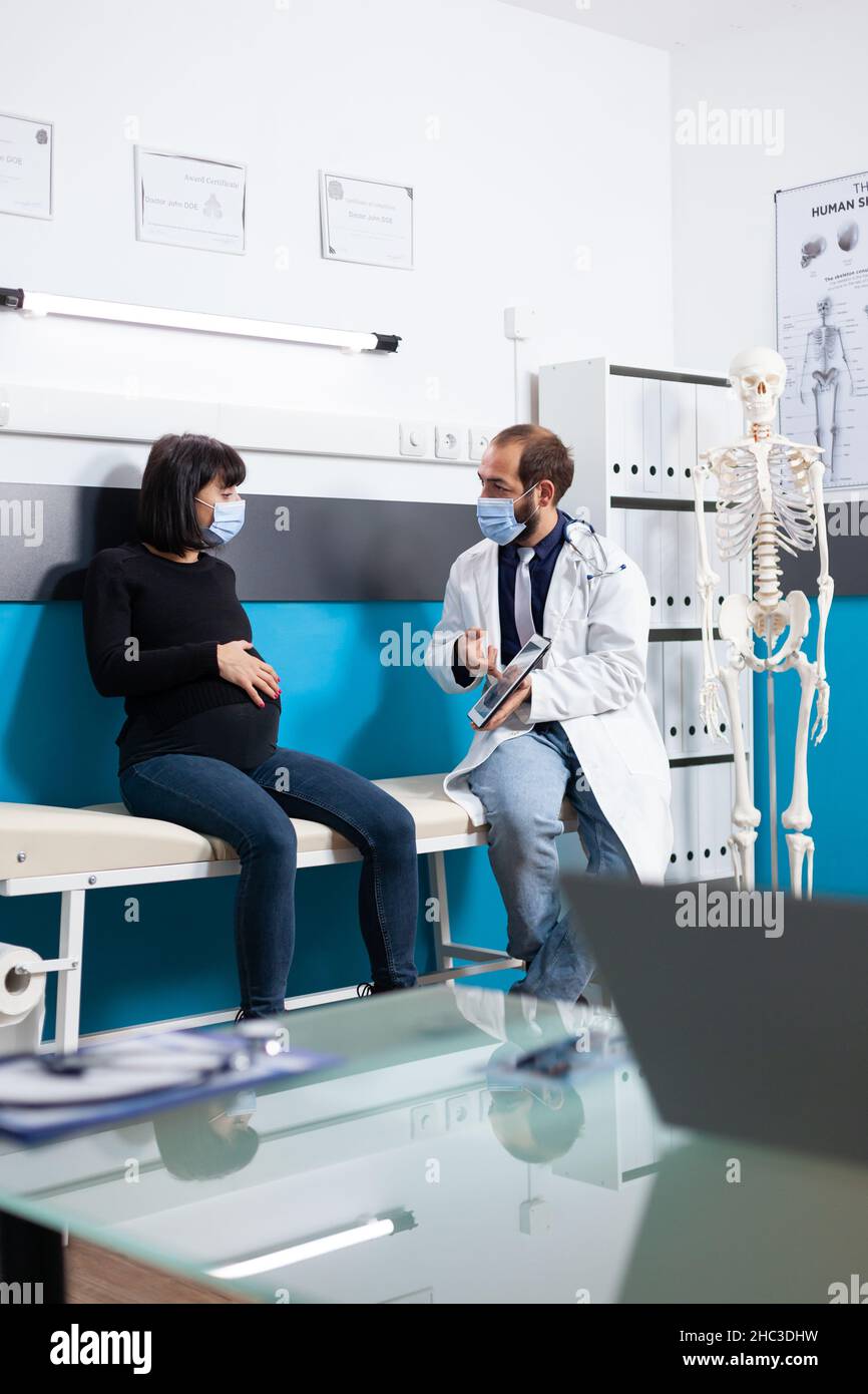 Woman expecting child looking at human skeleton on tablet with doctor ...