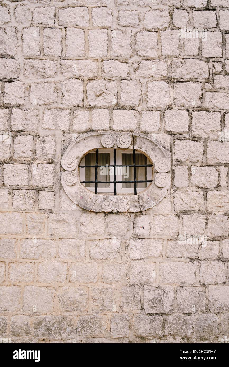 Small oval window with a lattice on the old stone facade of the ...