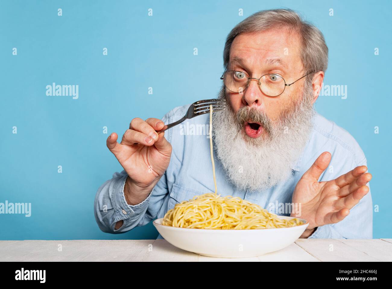 Shocked gray-bearded man is surprised by a large portion of noodles ...