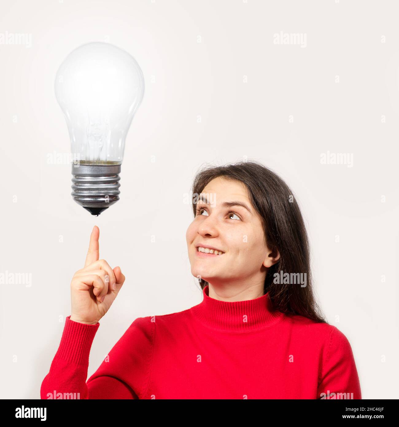A woman points her finger at a glowing light bulb while looking up ...