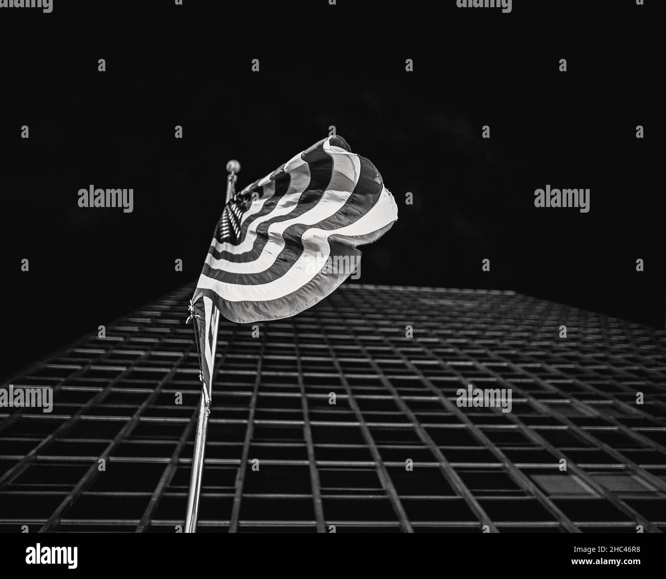 Low angle shot of the USA flag near a modern building in grayscale ...
