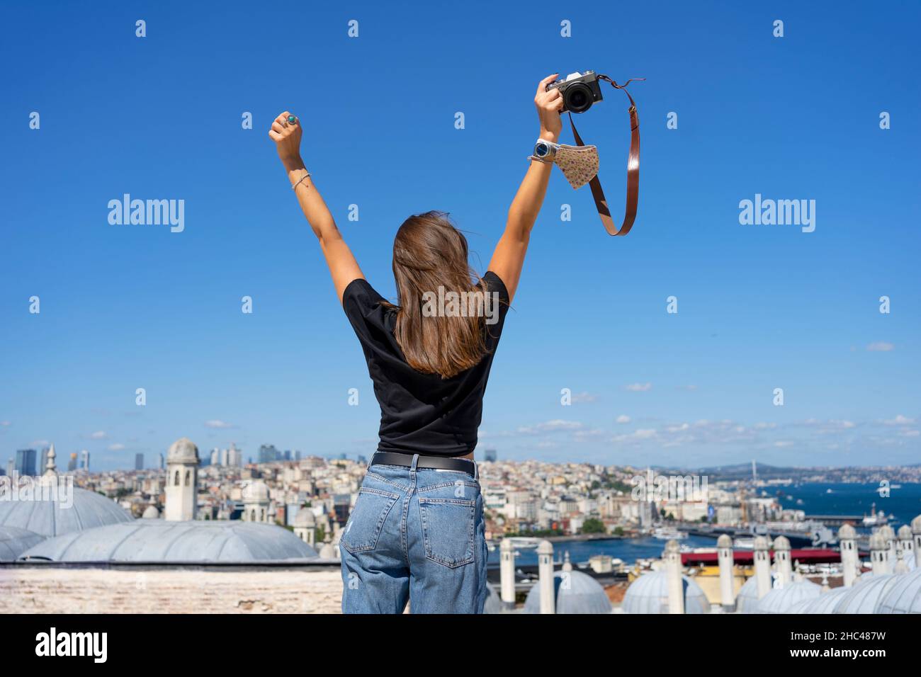 Back view of a photographer woman raising arms up towards the blue sky ...