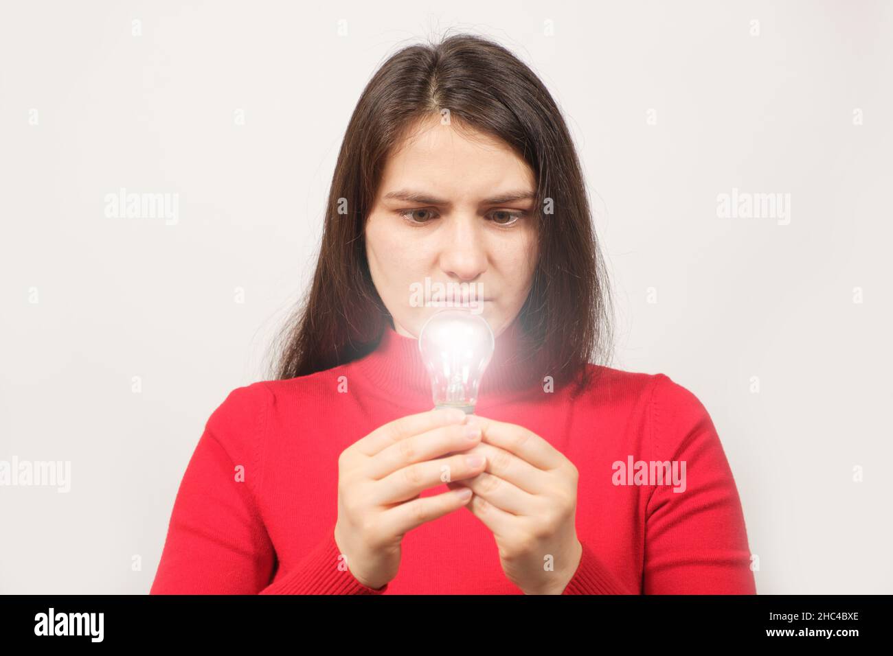 A Brunette Woman In Red Holds A Glowing Light Bulb In Her Hand Stock
