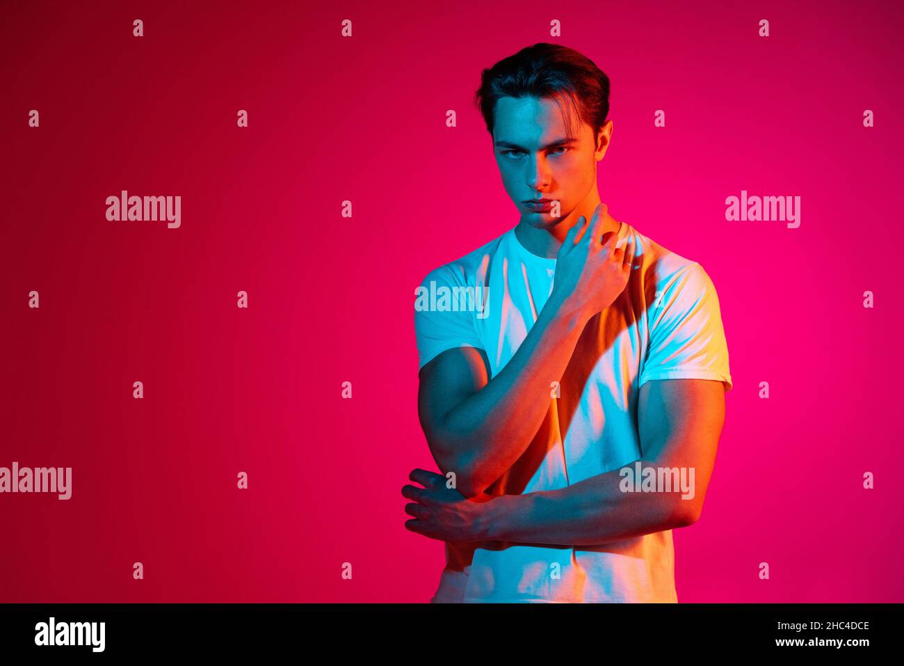 Young serious man posing isolated on magenta studio background in neon ...