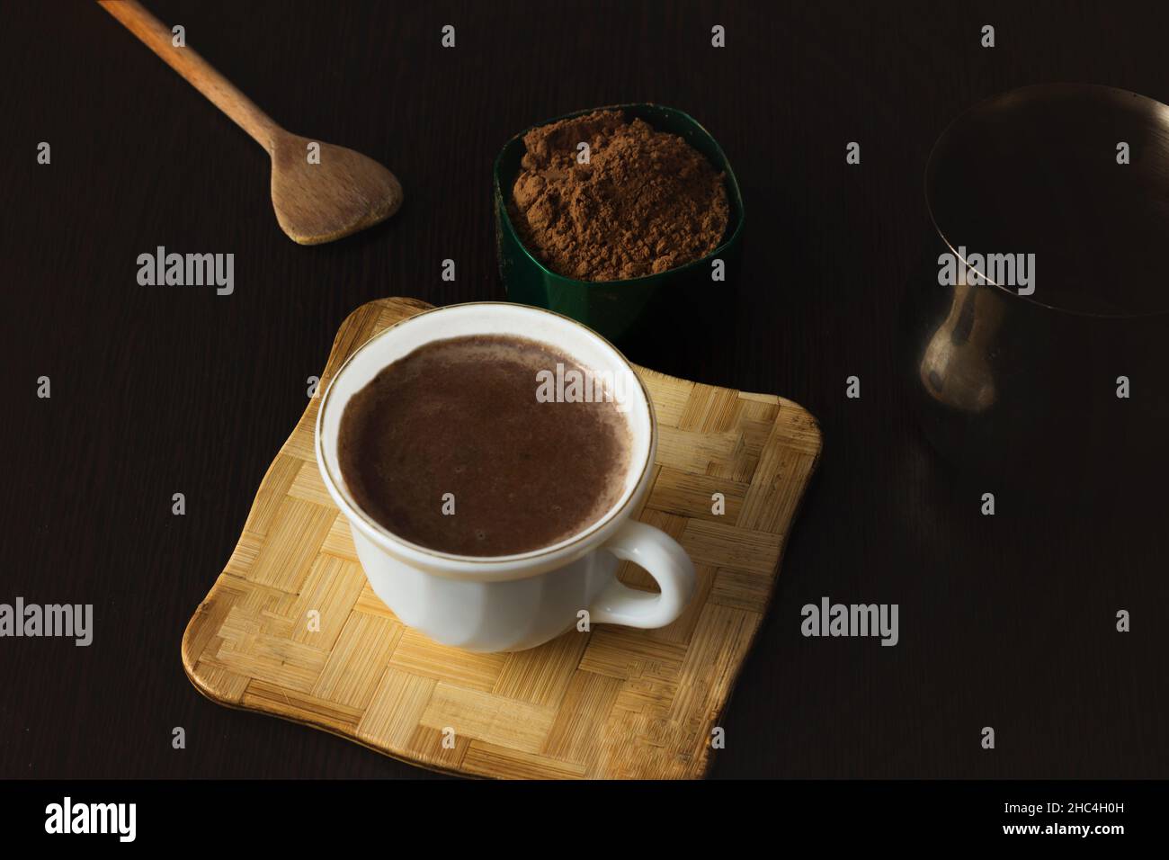 A cup with freshly brewed cocoa drink and a vessel standing next to it ...