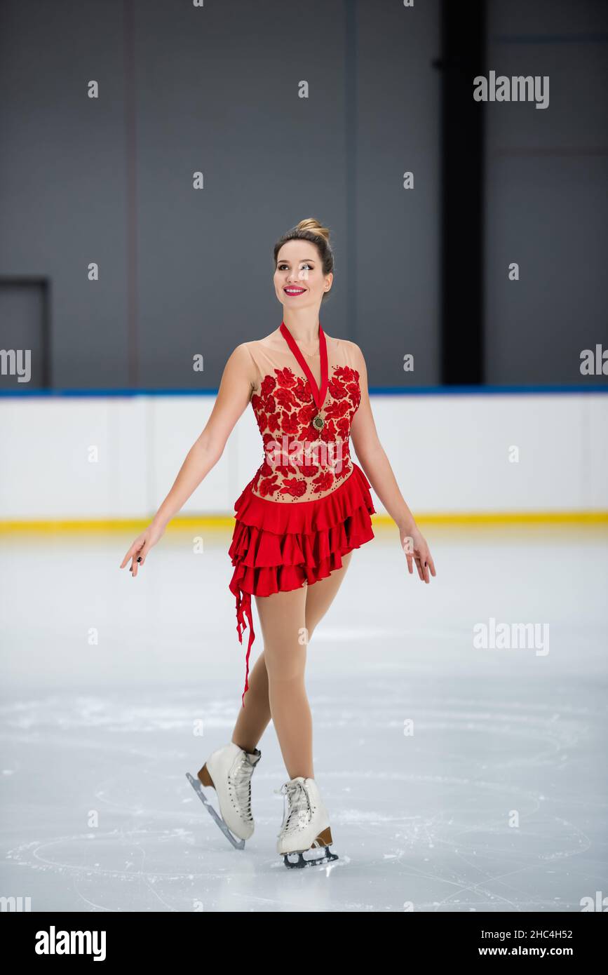 full length of happy figure skater in red dress with golden medal ...