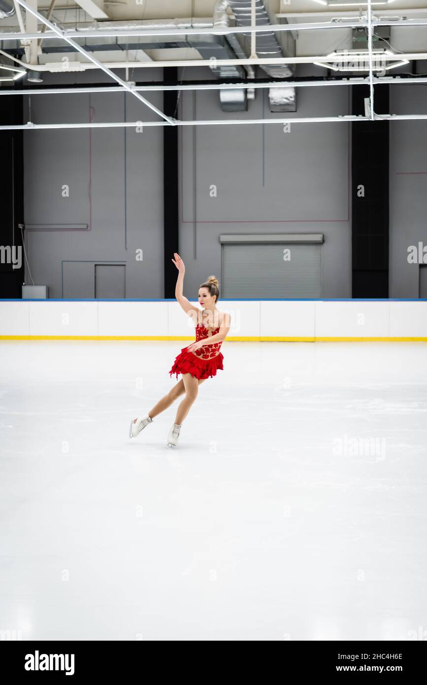 full length of young woman figure skating and gesturing in professional ...
