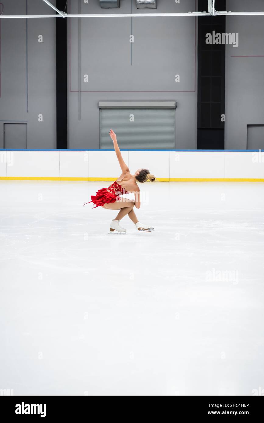 full length of young woman with outstretched hand figure skating in ...