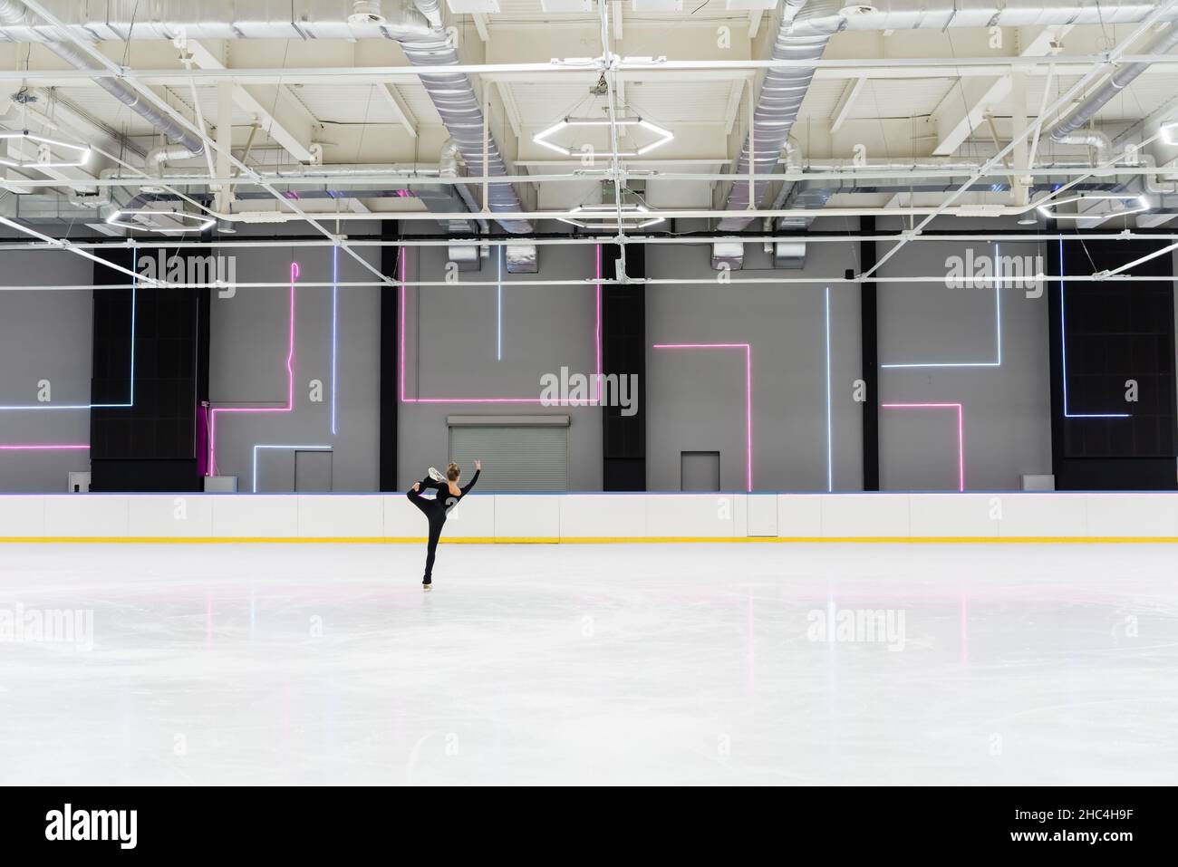 back view of young woman in black bodysuit skating in professional ice ...