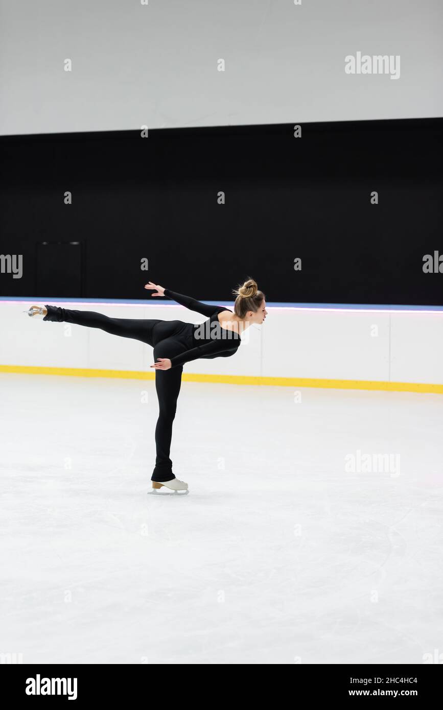 side view of professional figure skater in black bodysuit skating with ...