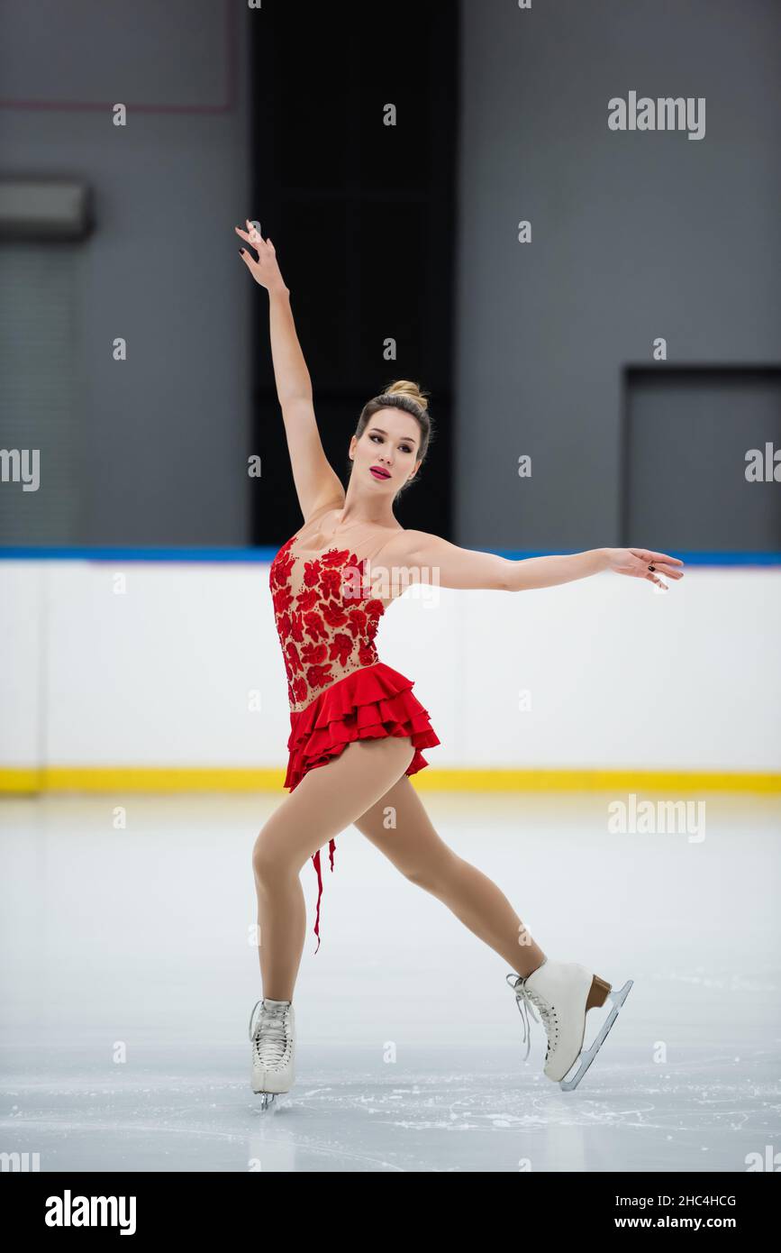 full length of woman in red dress figure skating with outstretched ...