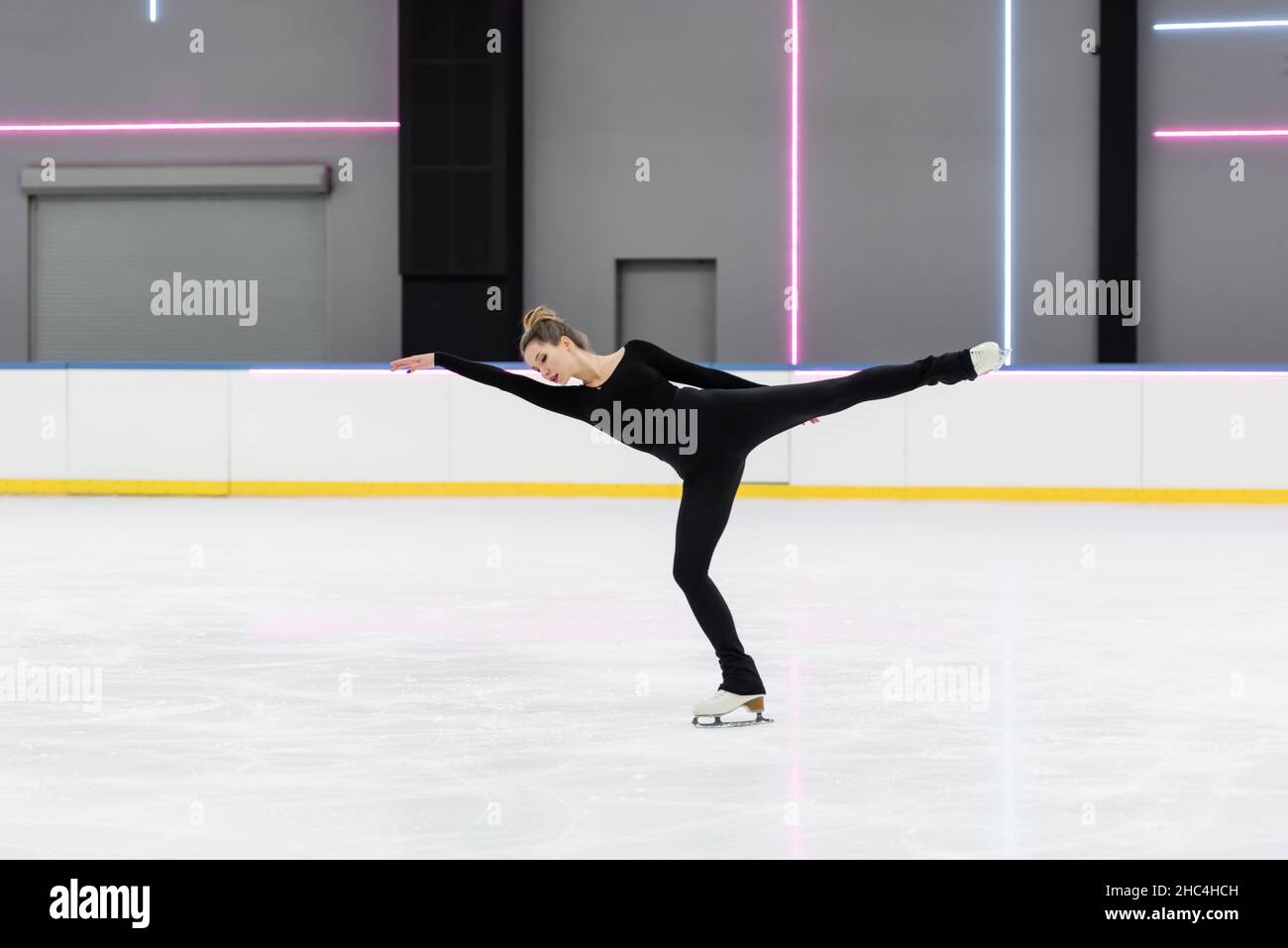 full length of young figure skater in black bodysuit skating with ...