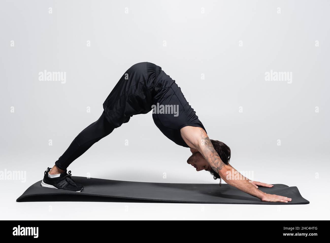 Side view of sportsman bending while stretching on fitness mat on grey ...