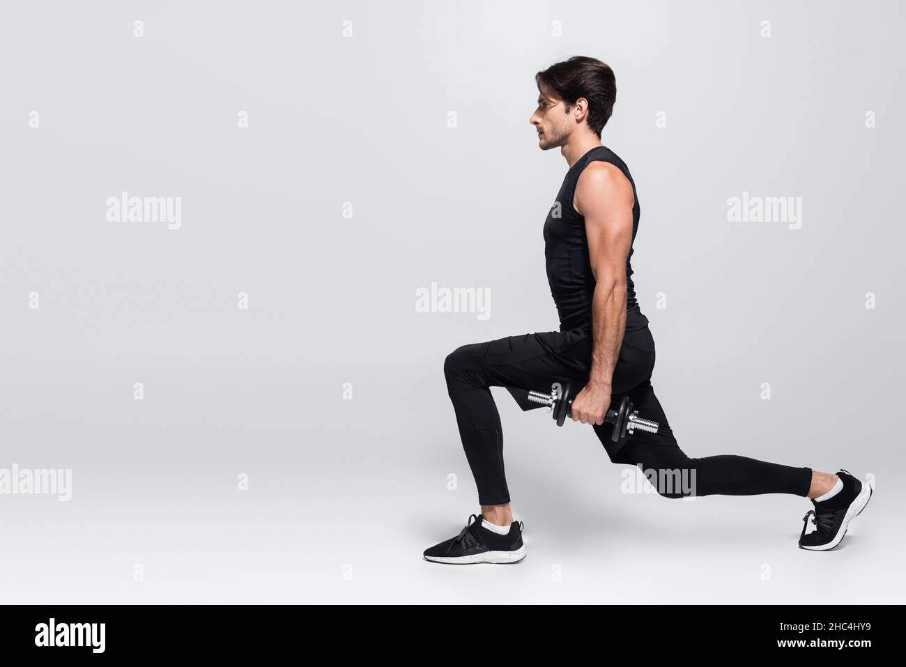 Side view of fit man training with dumbbell on grey background Stock ...