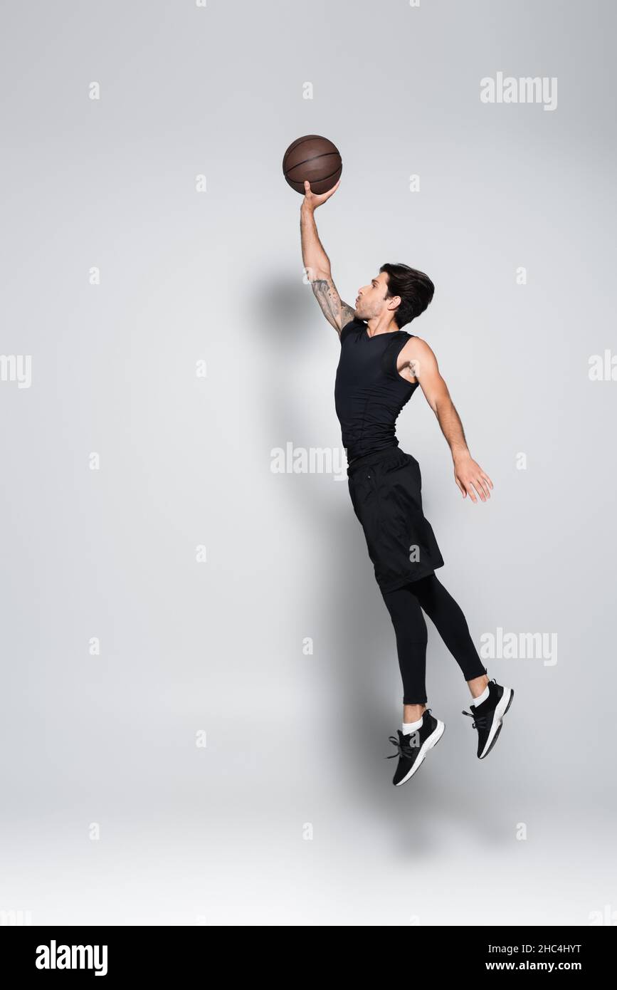 Side view of player with basketball ball jumping on grey background ...