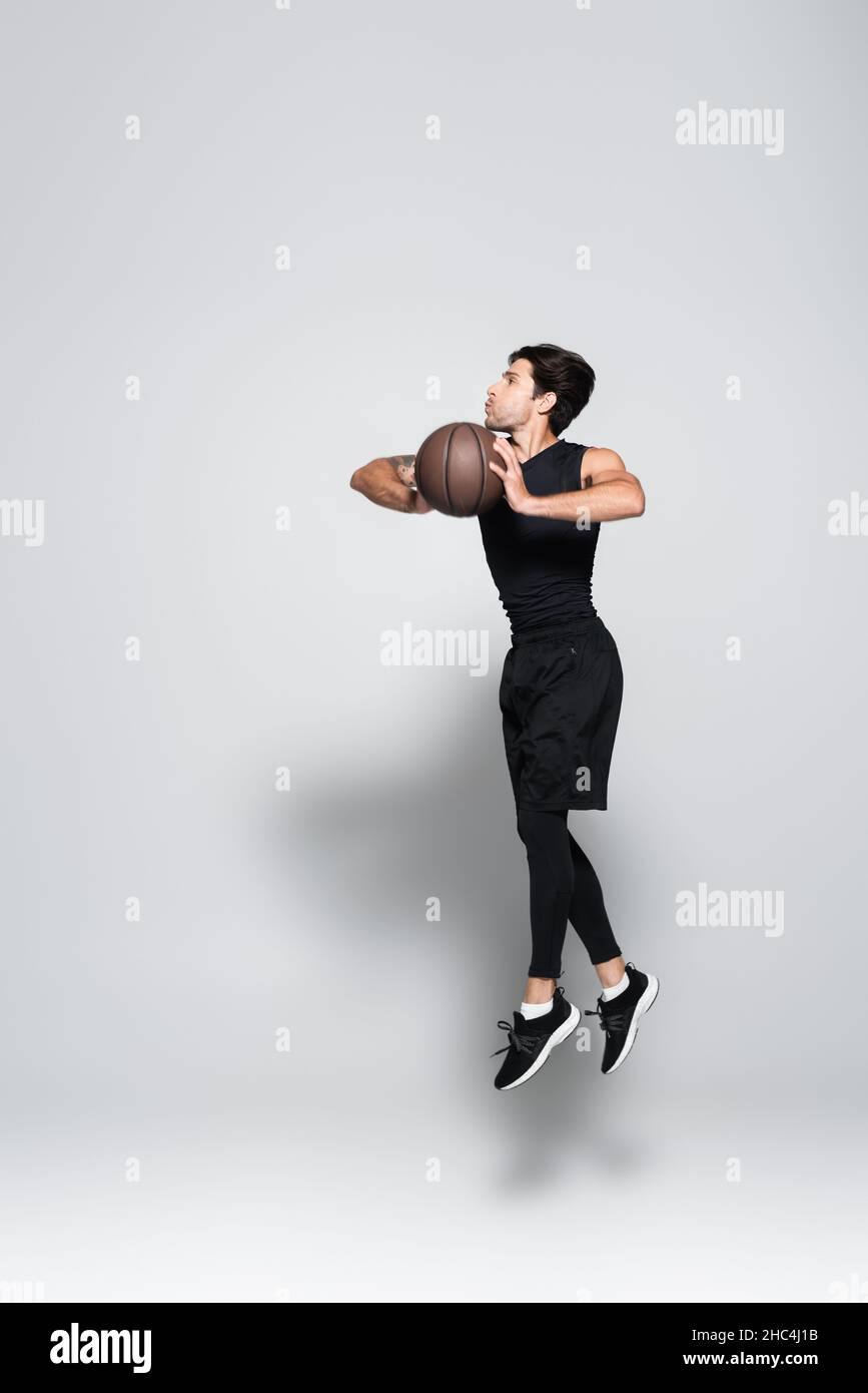 Side view of basketball player with ball jumping on grey background ...