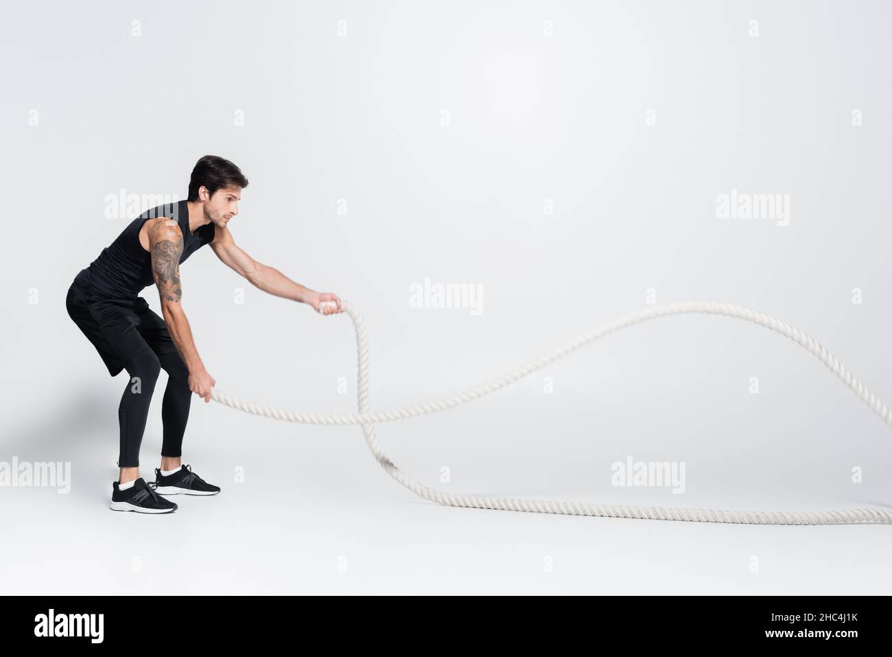 Side view of athletic sportsman holding battle ropes during cross ...