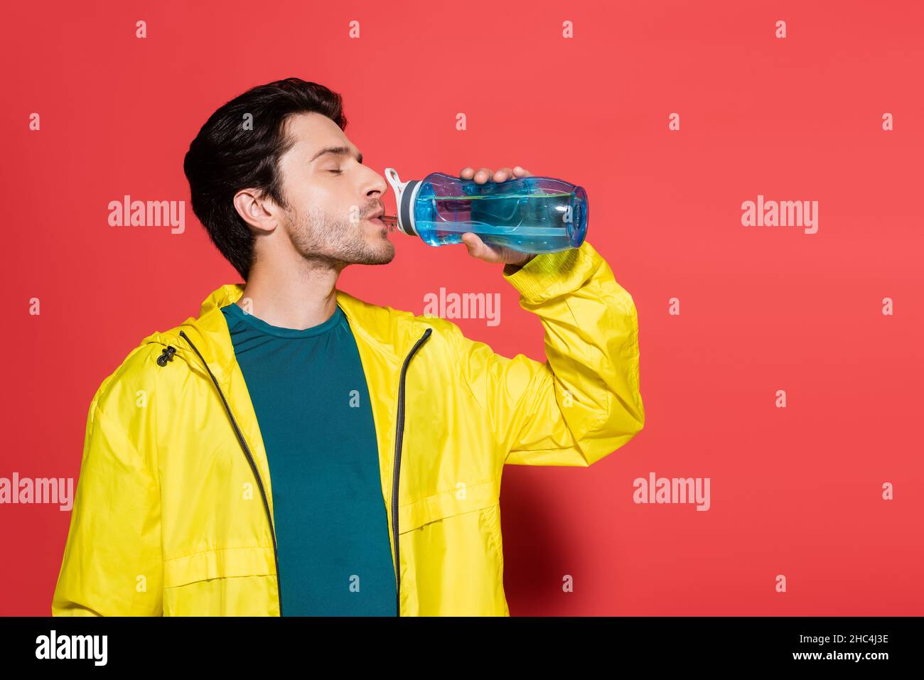 Sportsman in yellow sports jacket drinking water on red background ...