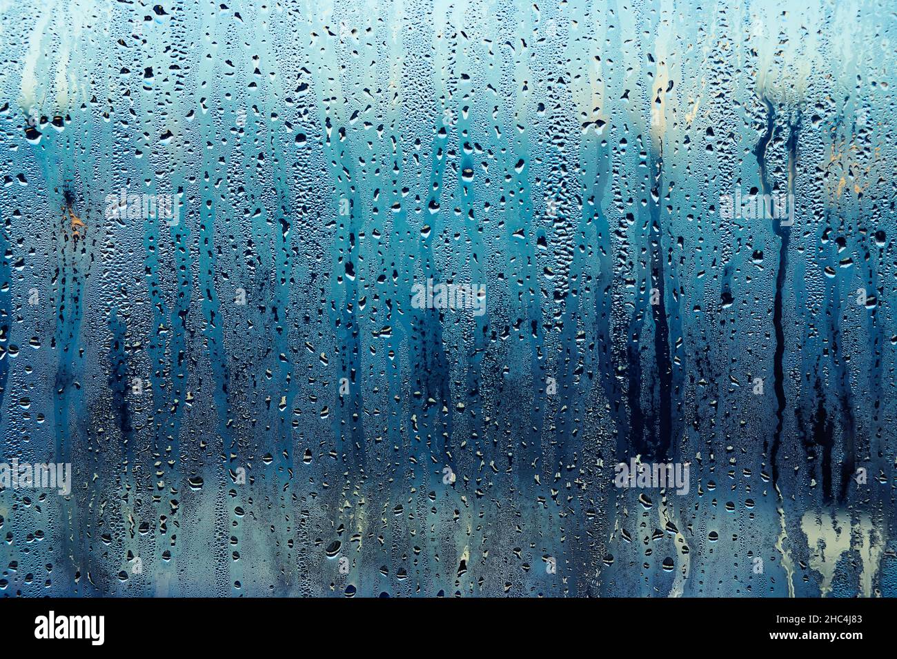 The transparent glass of the window is covered with dripping raindrops ...