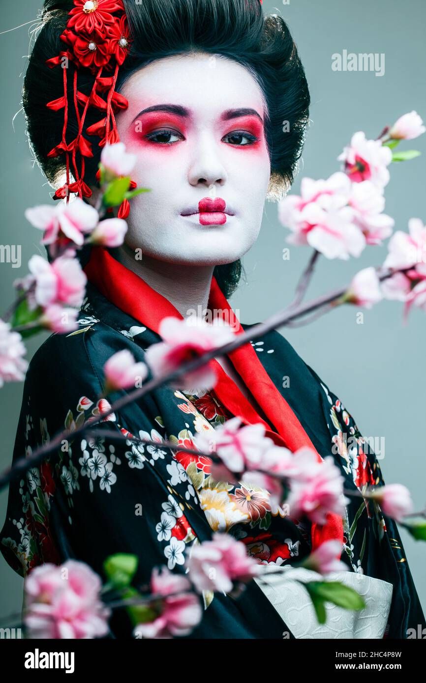 young pretty geisha in black kimono among sakura, asian ethno close up ...