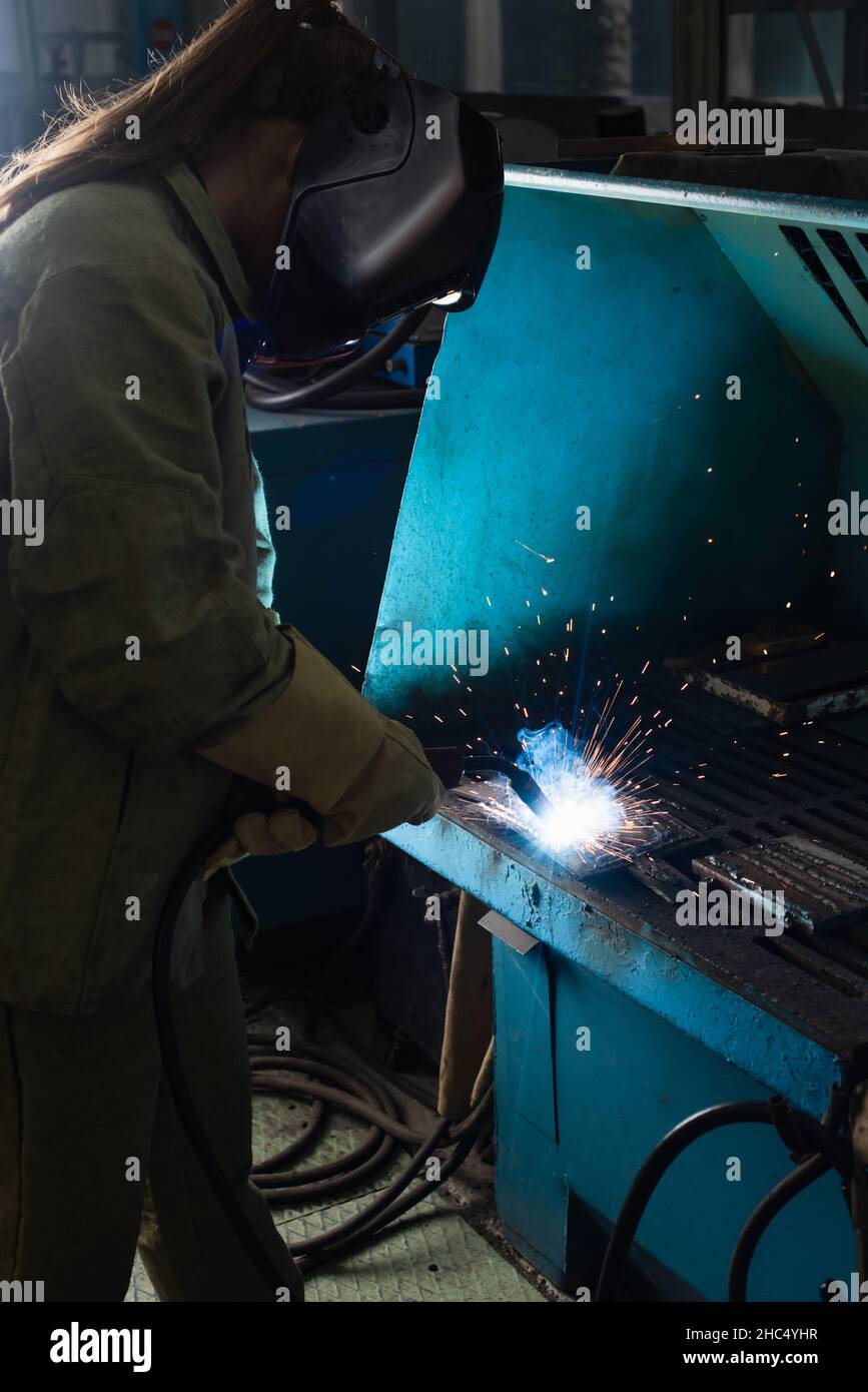 Young welder in uniform and protective mask working with welding torch ...