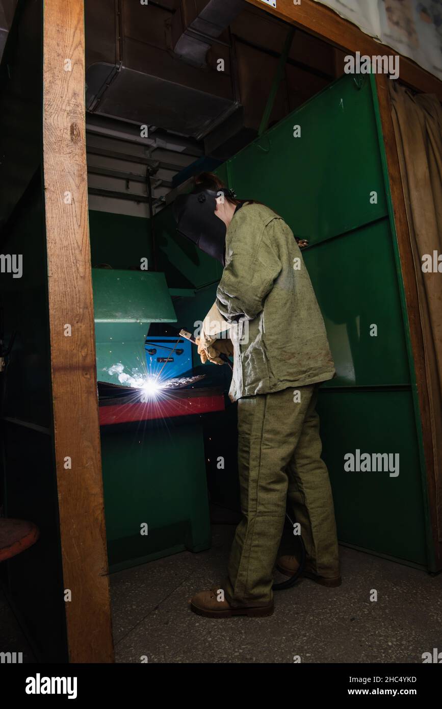 Full length of welder in protective uniform working with welding torch ...