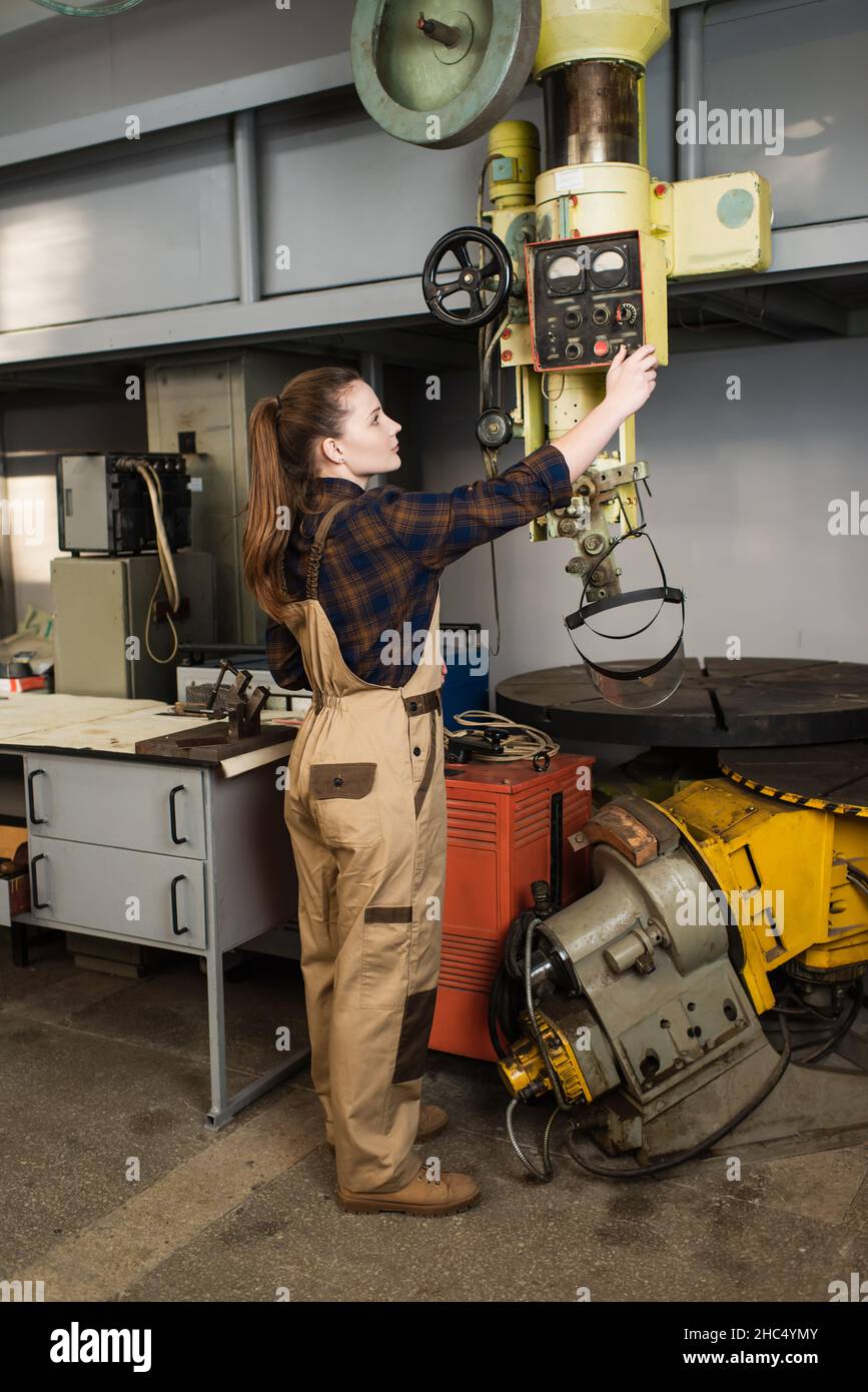 Side view of young welder in overalls tuning welding machine in factory ...