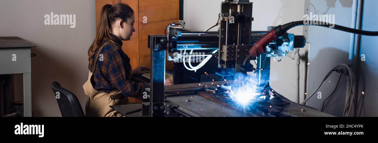 Side view of welder in overalls sitting near keyboard and welding ...
