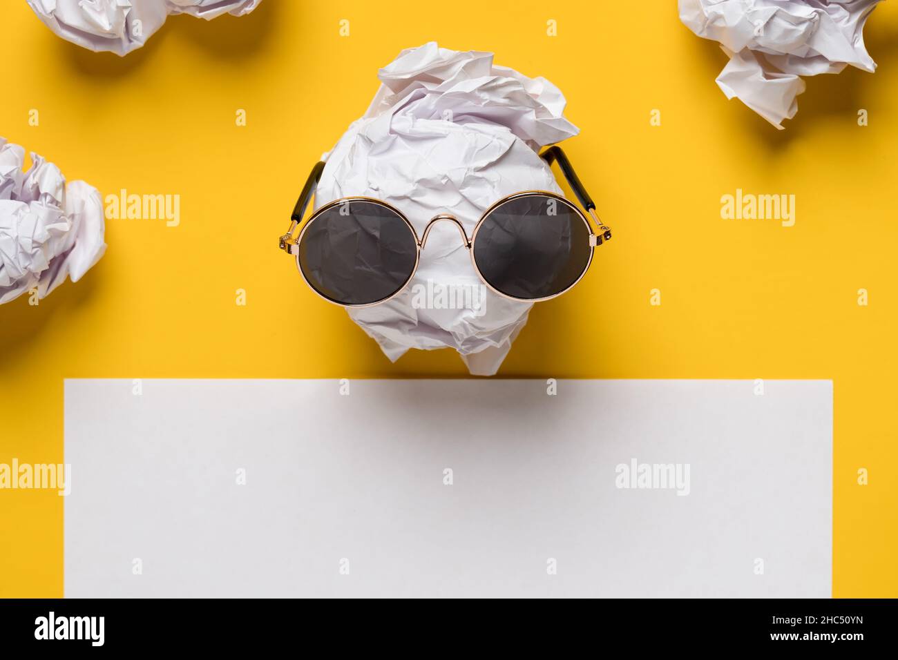 Crumpled paper and sunglasses on it look like a face, next to a white ...