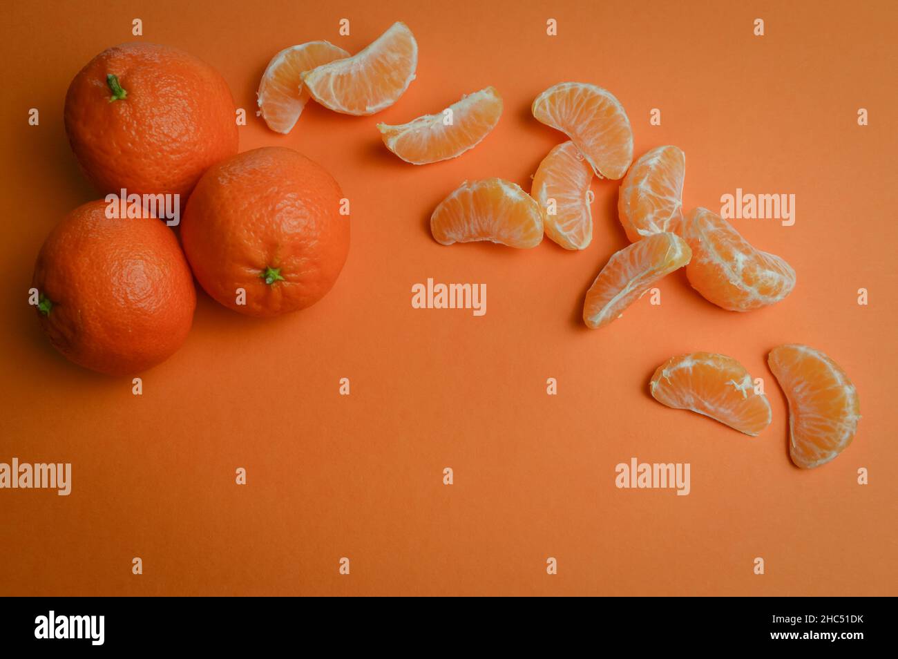 group of three organic tangerines and fruit wedges on an orange paper ...
