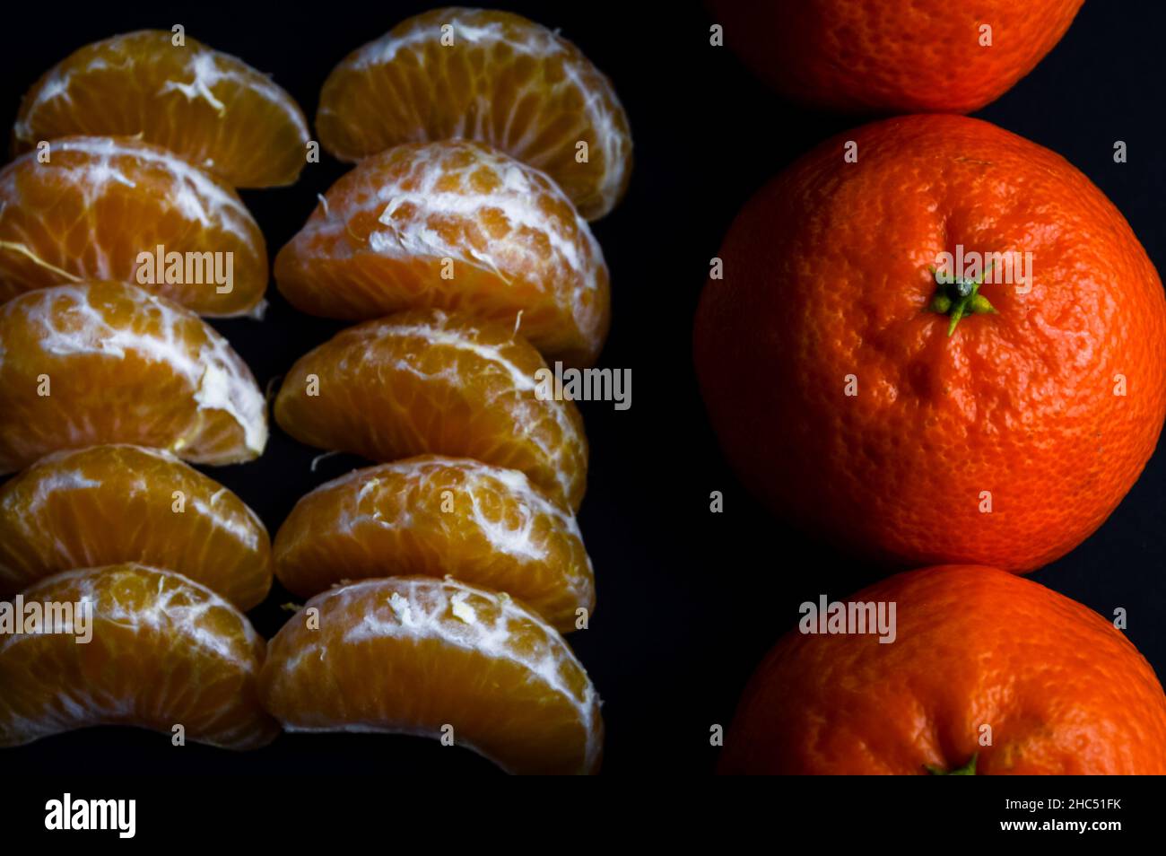 Whole organic tangerines with tangerine wedges lined up on black paper ...