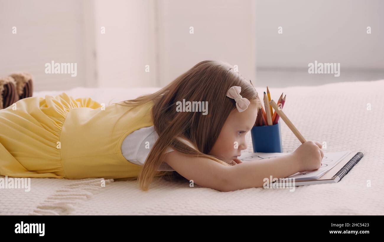 Side view of kid drawing on paper while lying on bed Stock Photo - Alamy