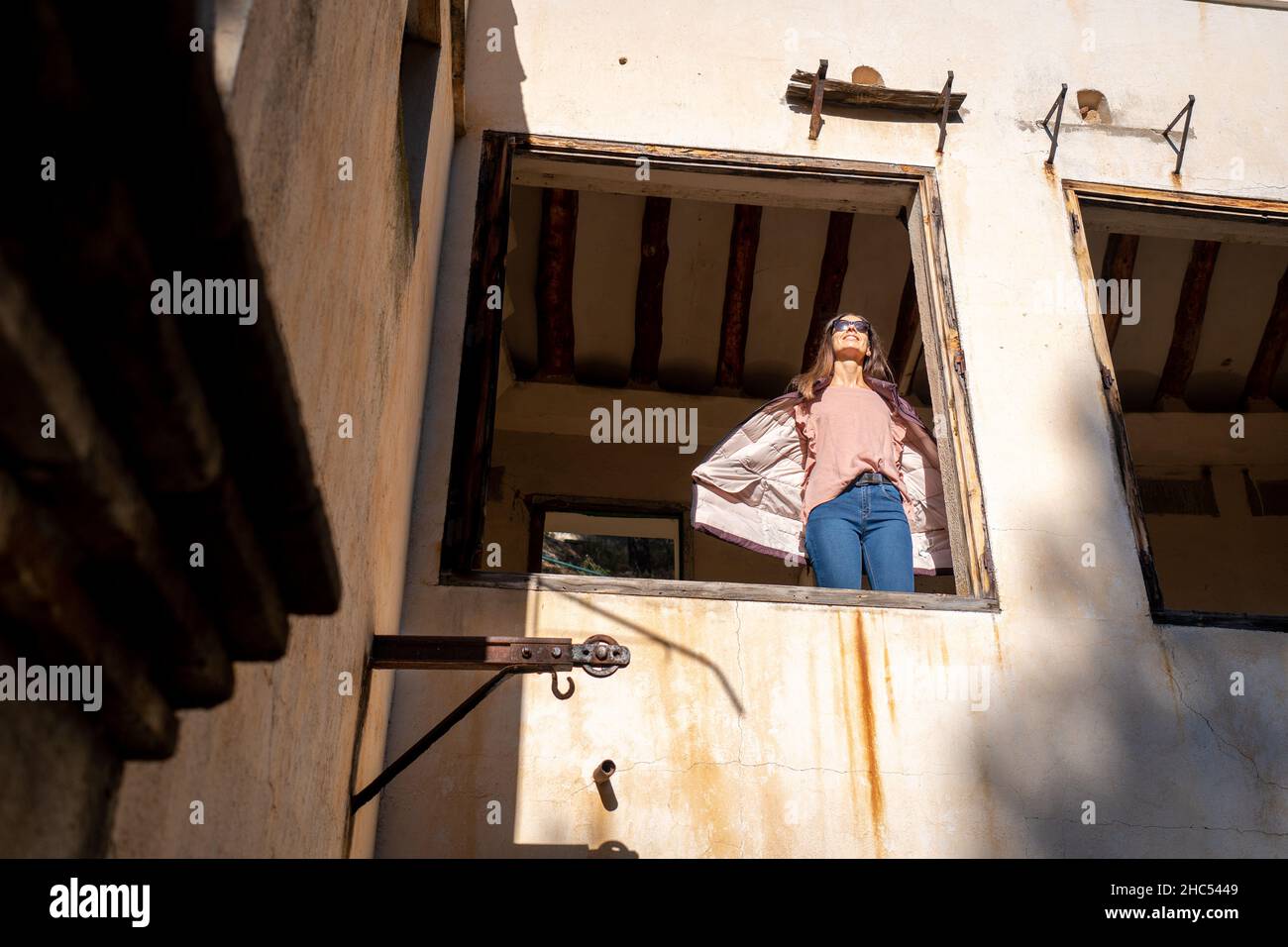 Young woman leaning out of a window of a dilapidated room on a sunny ...