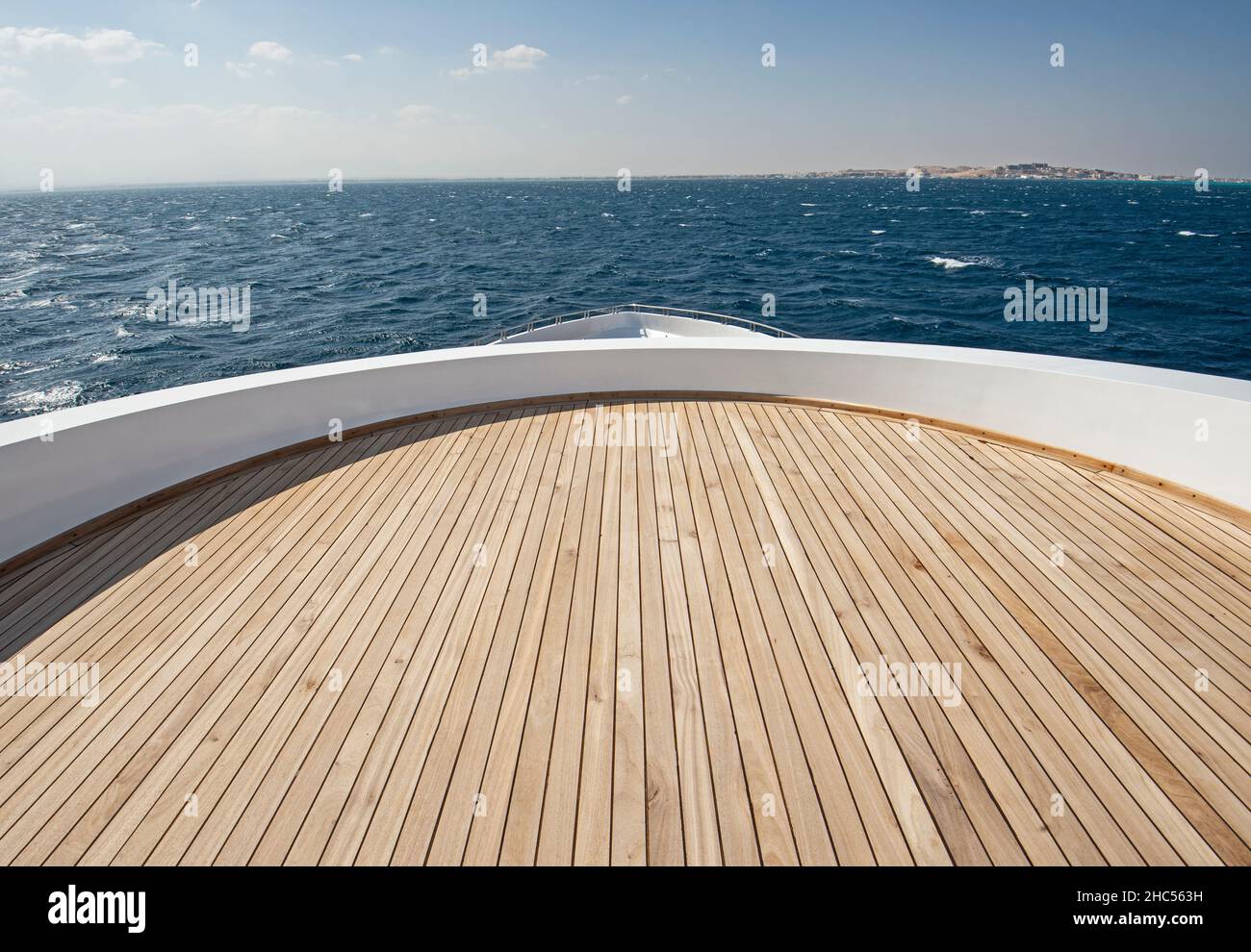 Teak bow deck of a large luxury motor yacht out at sea with a tropical ...