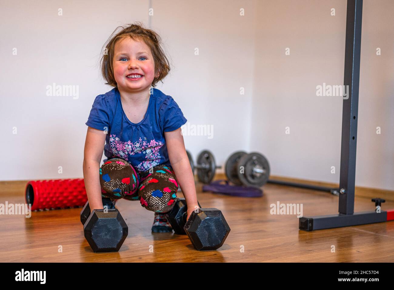 A cute four-year-old girl is pretending to do workout with dumbbells in ...
