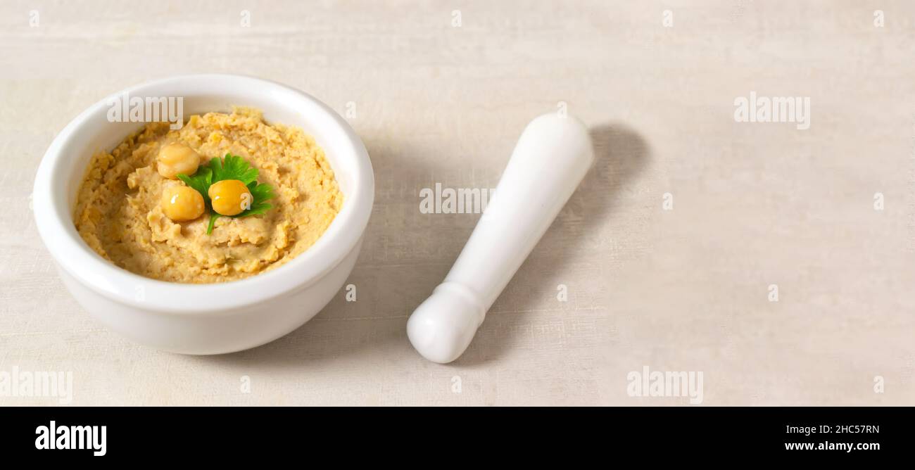 Hummus in a ceramic white bowl with a parsley leaf on a light ...